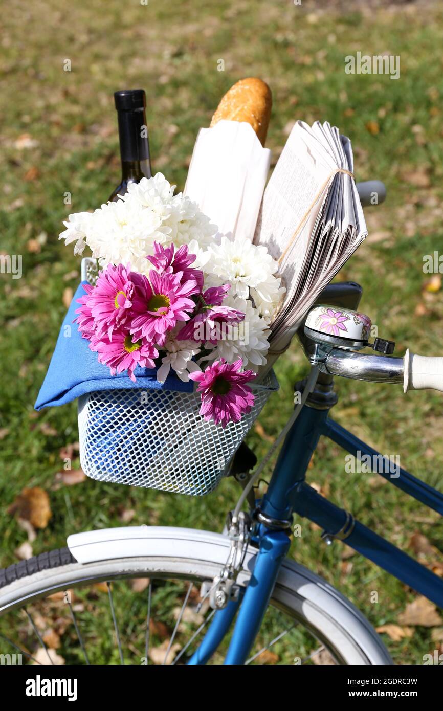 Bicycle with flowers, bread and bottle of wine in metal basket on grass ...