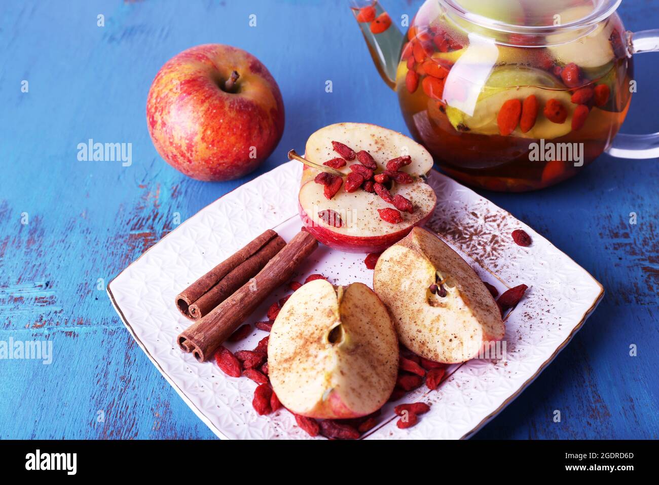 Ripe apple, goji berries and cinnamon on white square plate and fruit ...