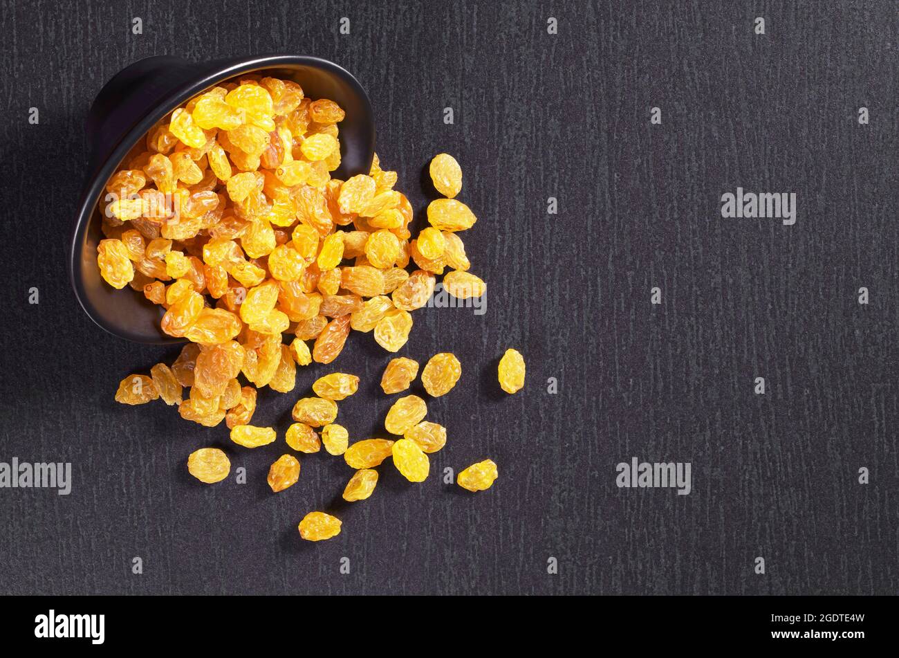 Golden raisins in bowl and scattered on black stone background, top ...