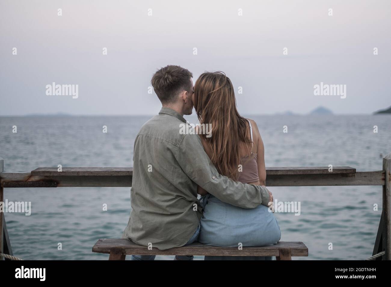Back side view of the loving couple sitting on the bench near the sea ...