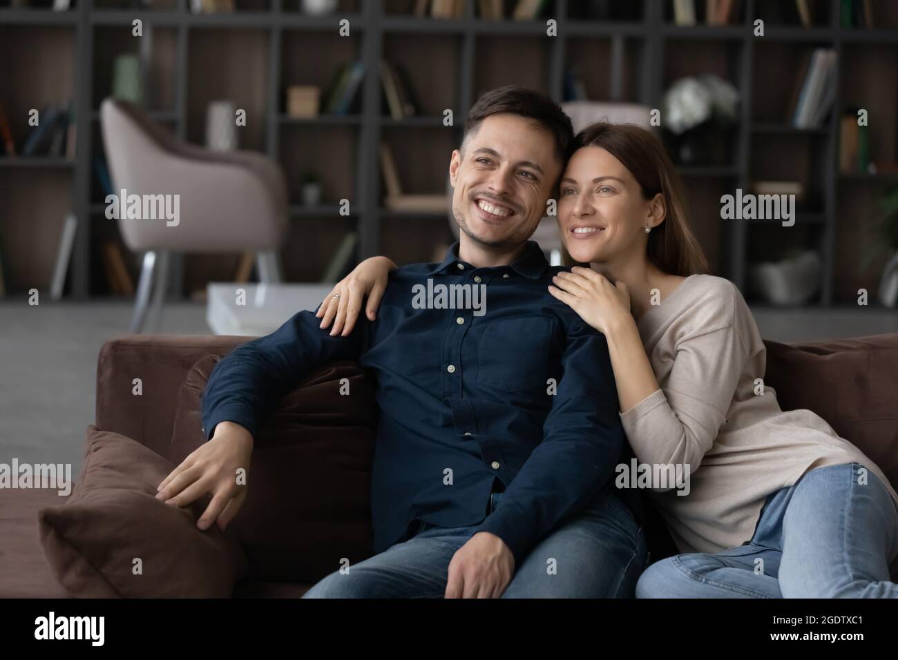 Dreamy couple looking in distance hugging relax together on sofa Stock ...