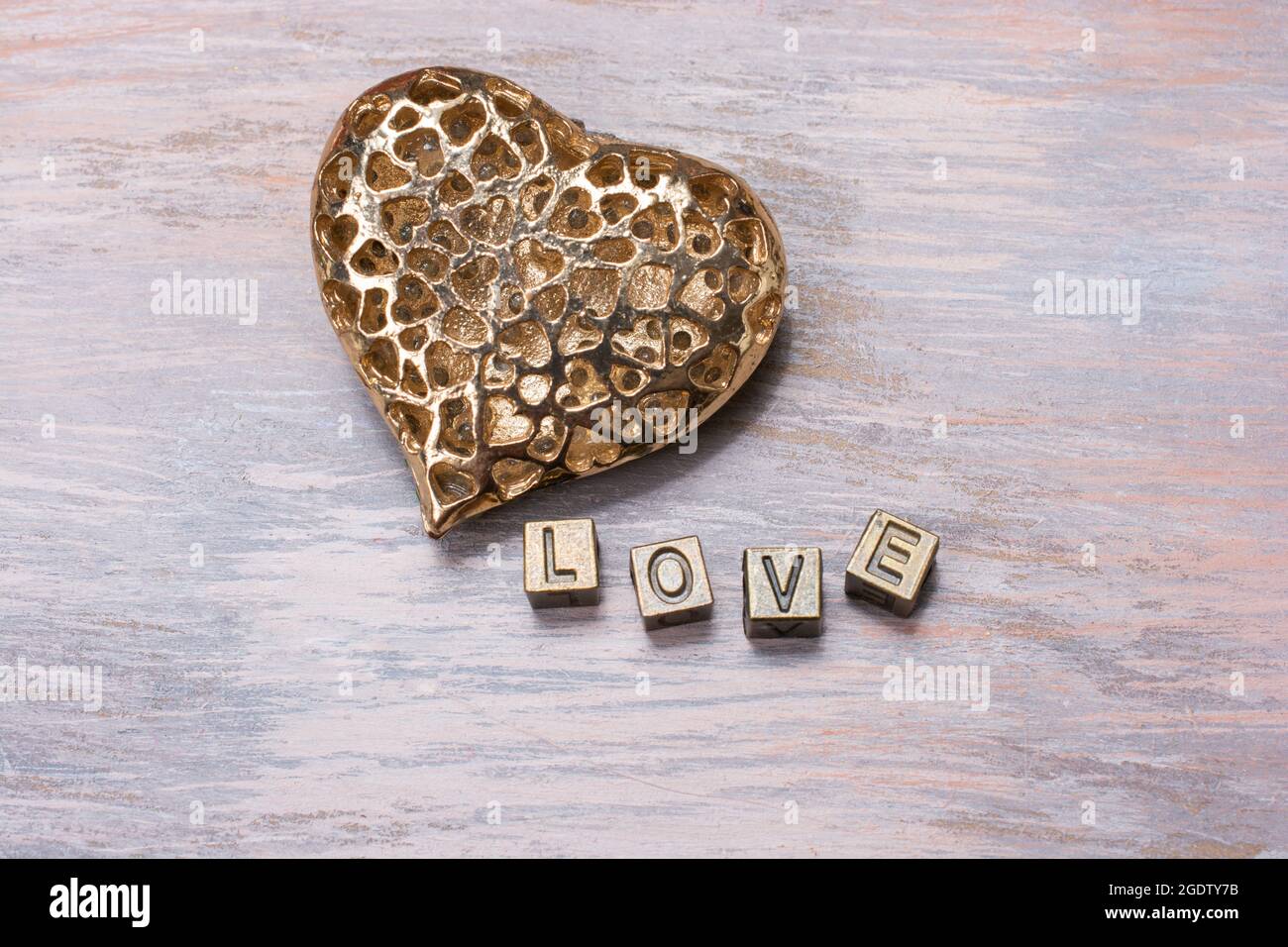 A heart shaped gold color metal and a word LOVE on a surface with faded ...