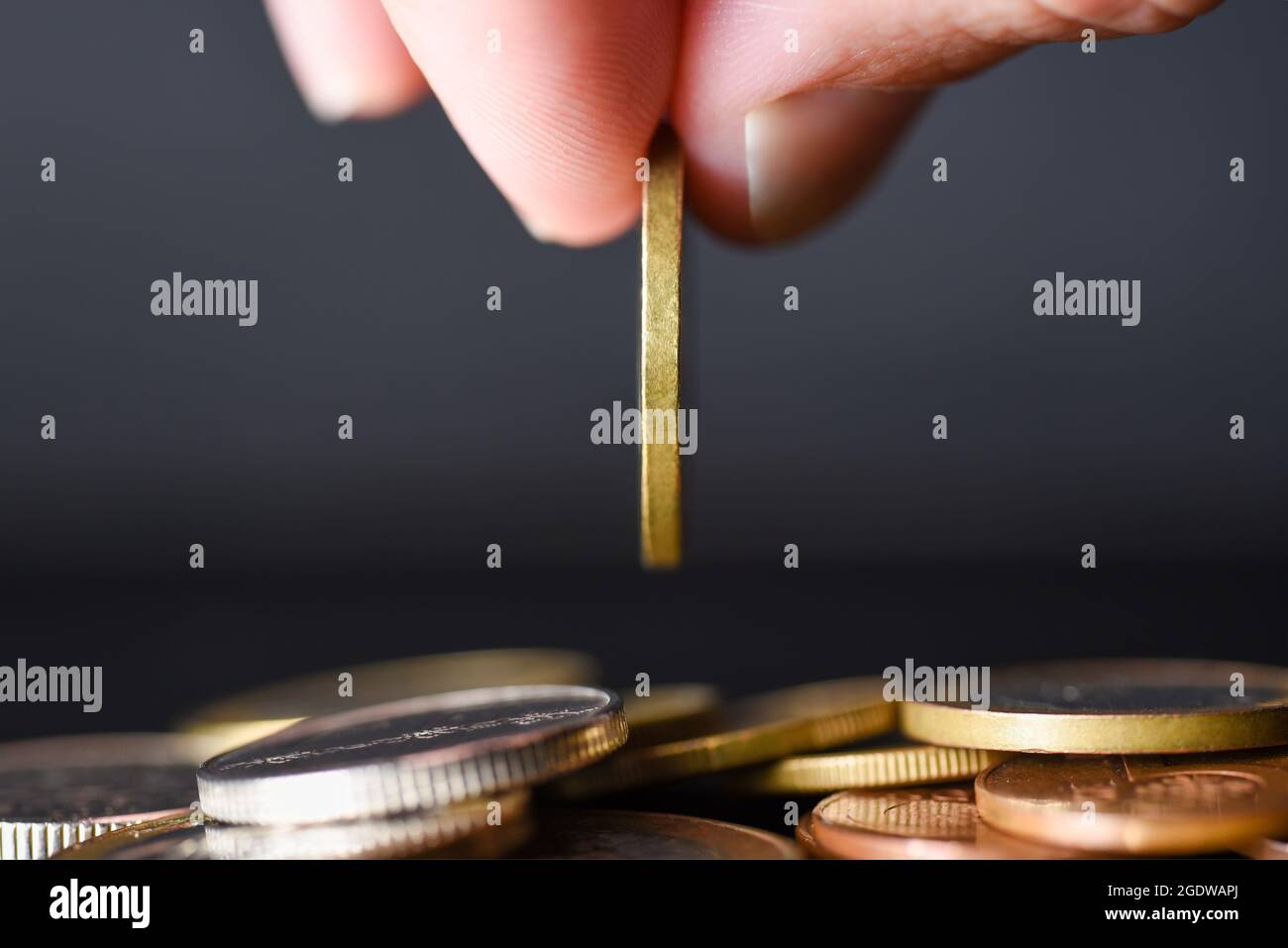 Hand drops a coin into a stack of coins on a black background Stock ...