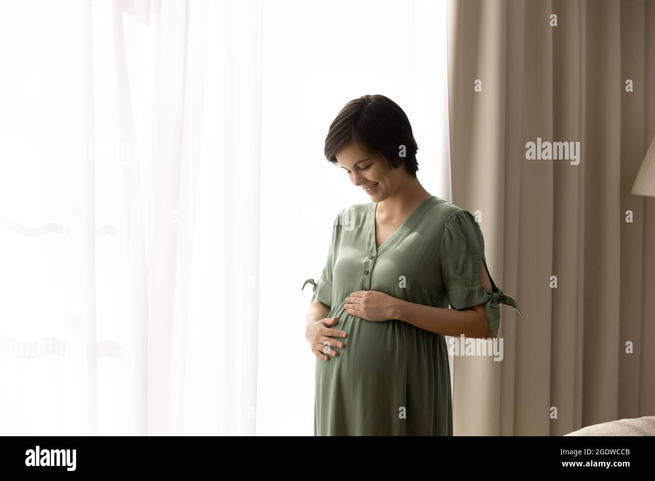 Happy young pregnant woman wearing stylish dress, touching big belly ...