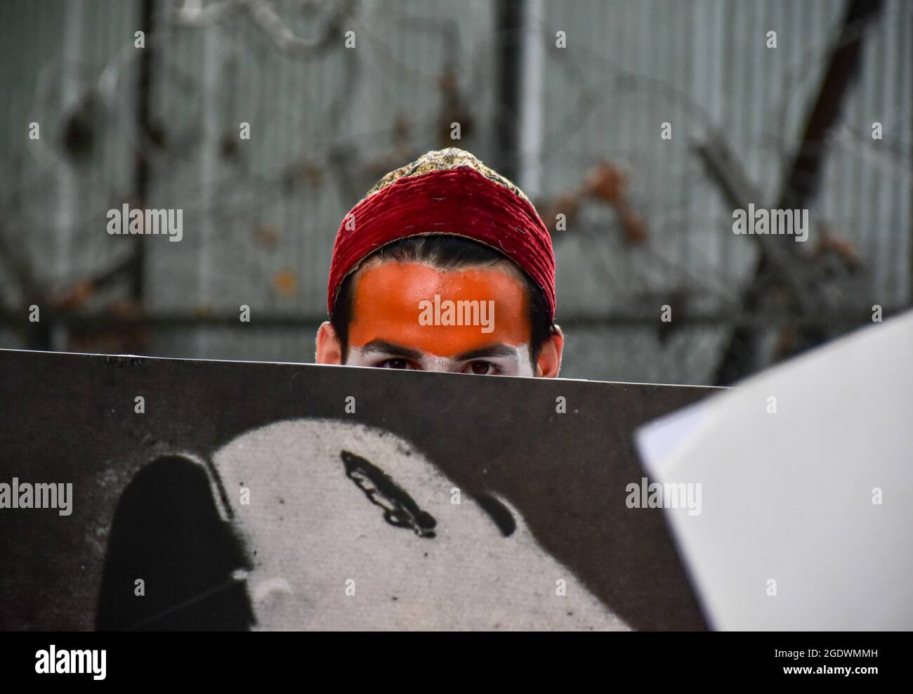 A boy with his face painted in colors of the Indian flag hides behind a ...