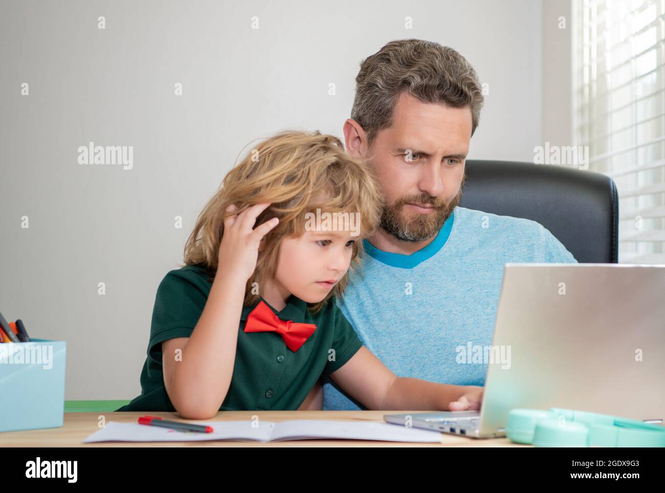 bearded dad or school private tutor teaching boy son with modern laptop ...