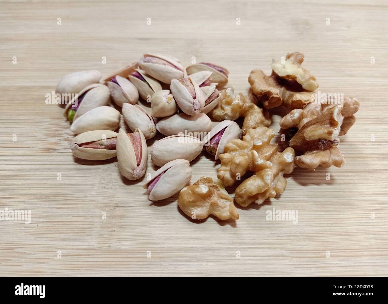 A closeup shot of a pile of peeled walnuts and pistachios on a wooden ...