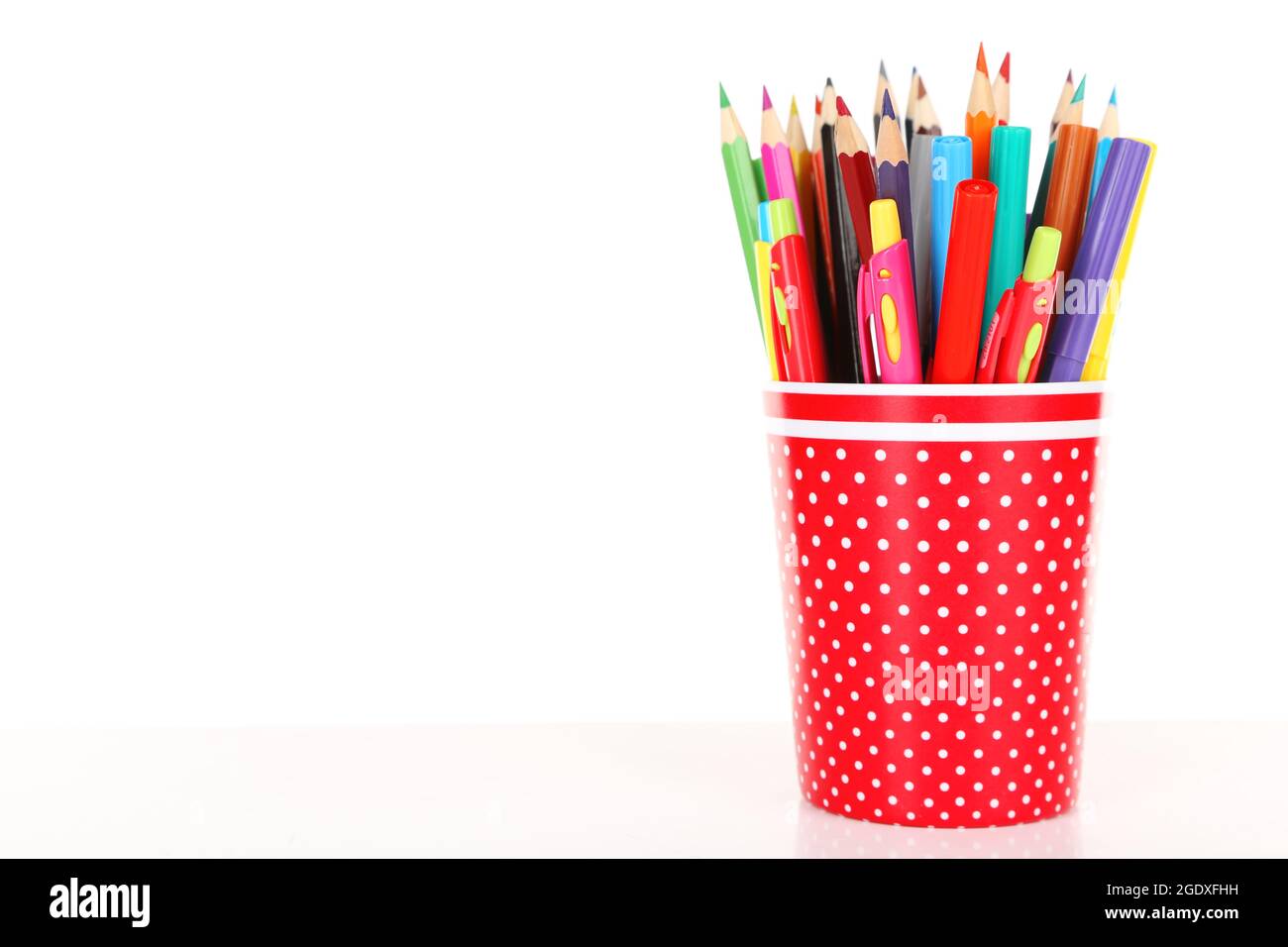 Colorful pens, pencils and markers in red polka-dot plastic cup ...