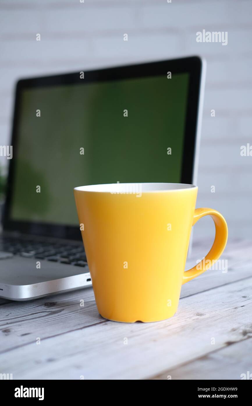 yellow color coffee mug and laptop a on table Stock Photo - Alamy