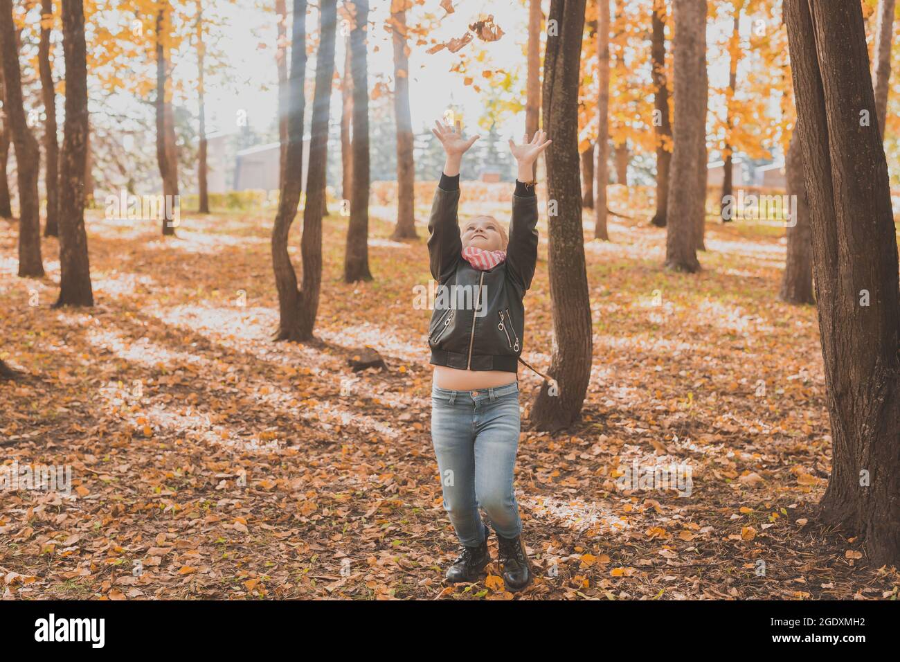 Happy child throwing the fallen leaves up playing in the autumn park ...