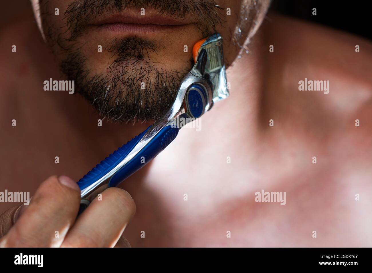 Handsome man shaving his beard with razor in bathroom. Daily cosmetic ...