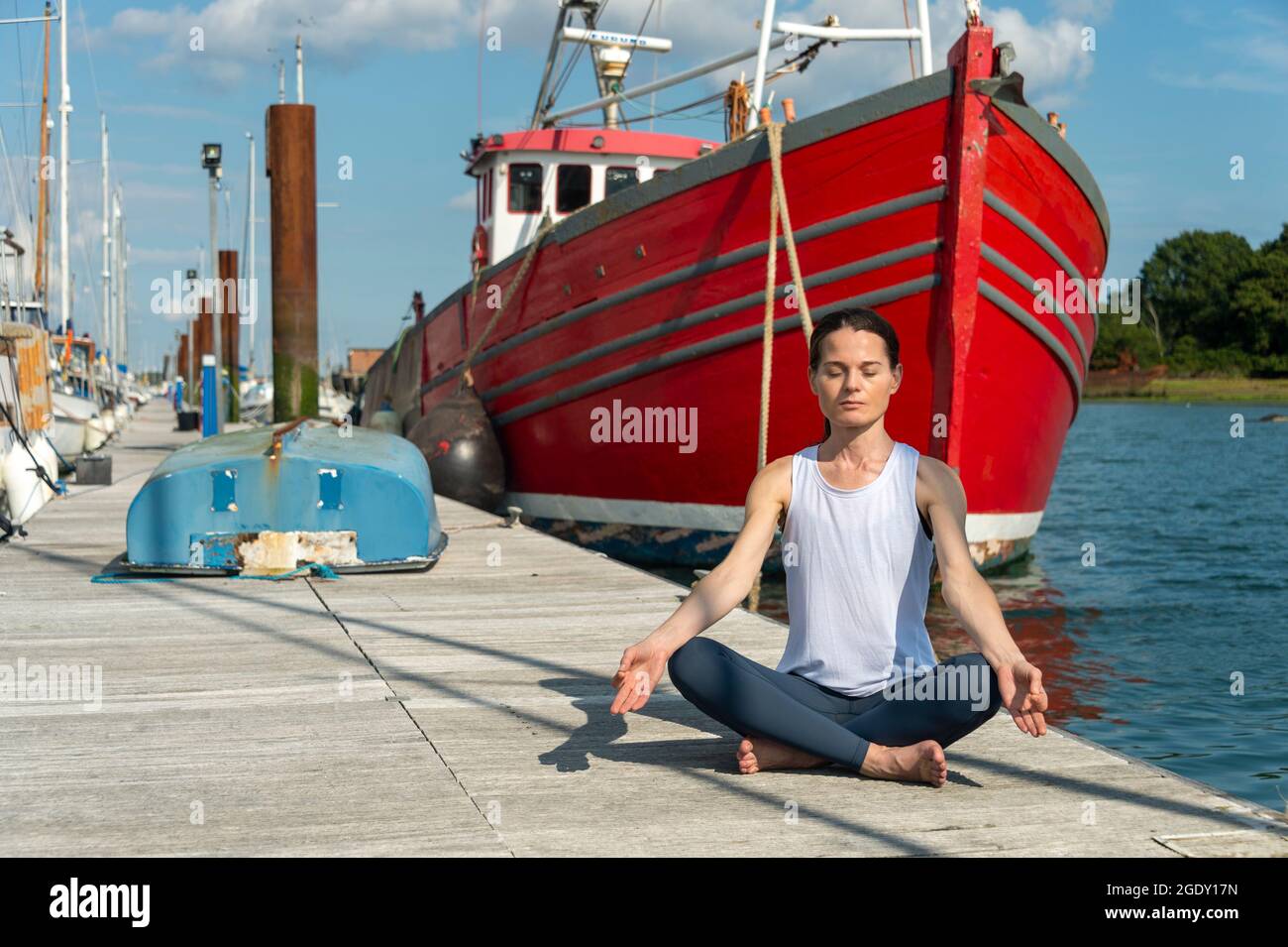 fit woman practicing yoga and meditation sitting on a pontoon with ...
