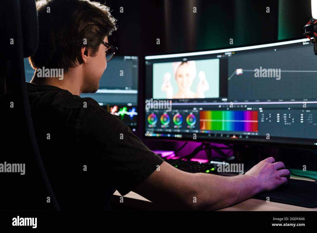 Back view of a young white man video editor sitting in front of a big ...