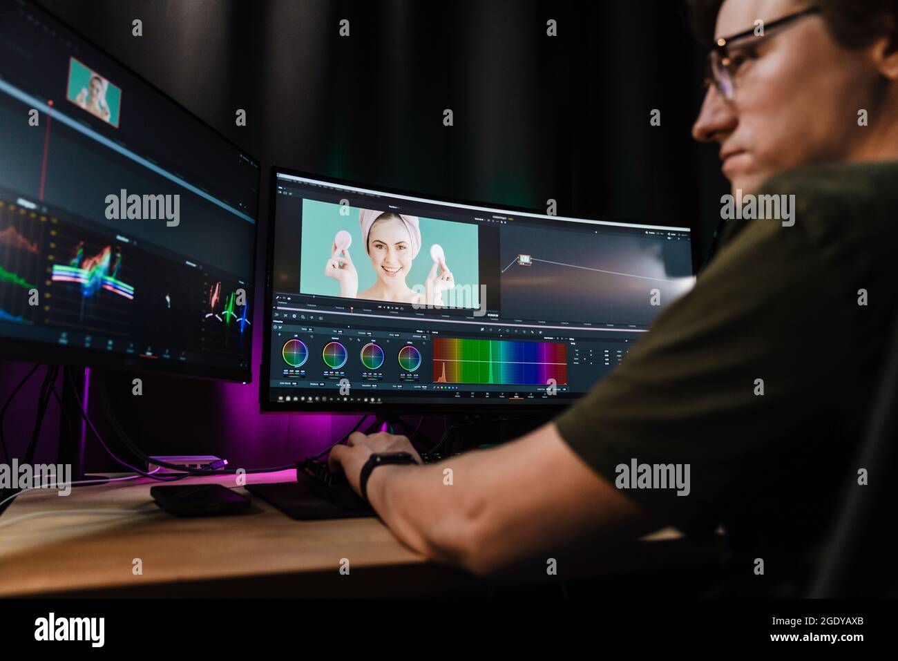 Back view of a young white man video editor sitting in front of a big ...