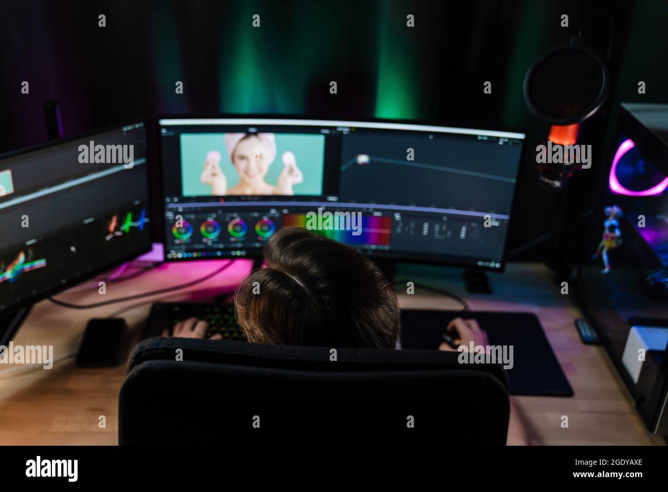 Back view of a young white man video editor sitting in front of a big ...