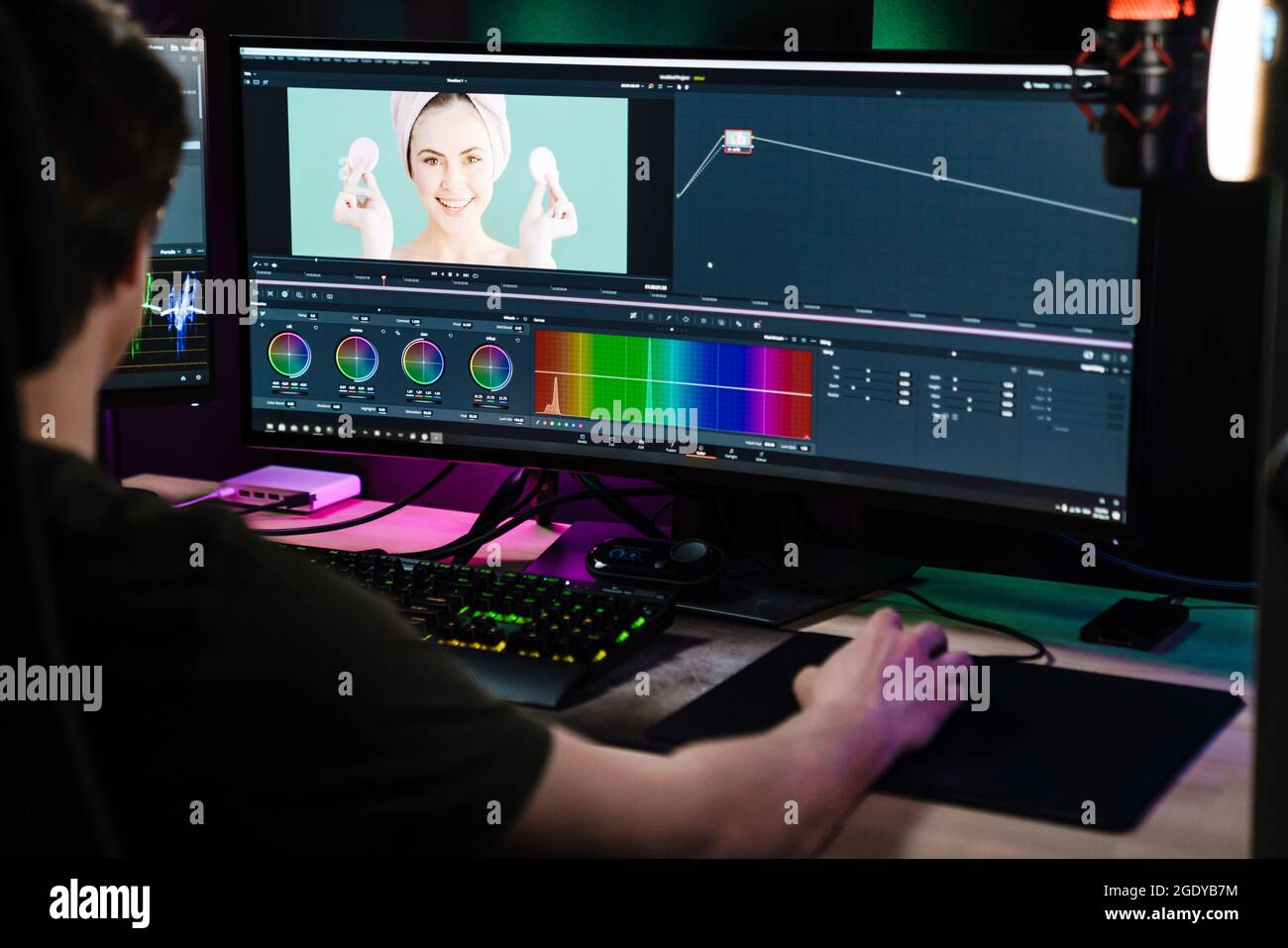 Back view of a young white man video editor sitting in front of a big ...