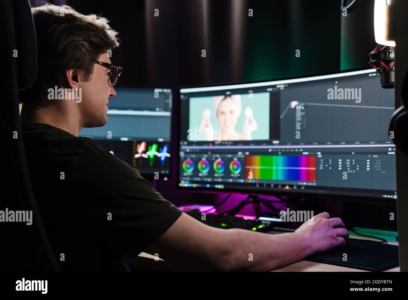 Back view of a young white man video editor sitting in front of a big ...