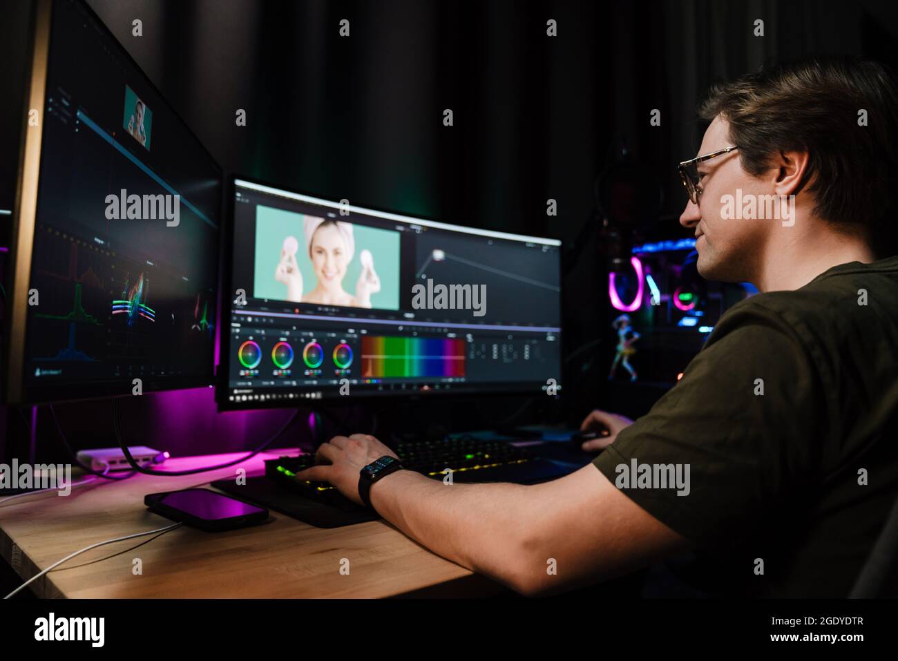 Back view of a young white man video editor sitting in front of a big ...