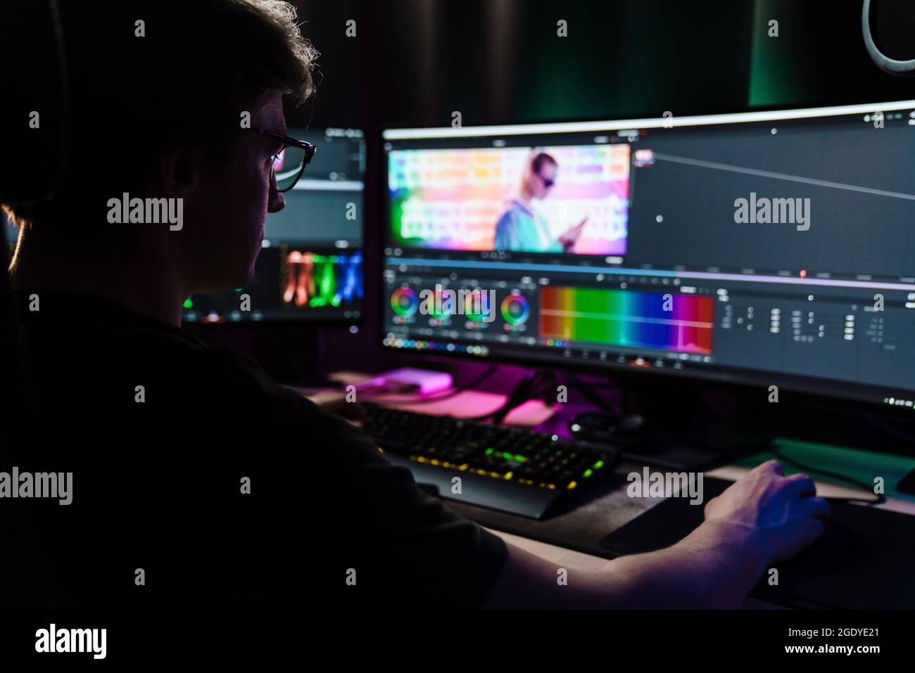 Back view of a young white man video editor sitting in front of a big ...