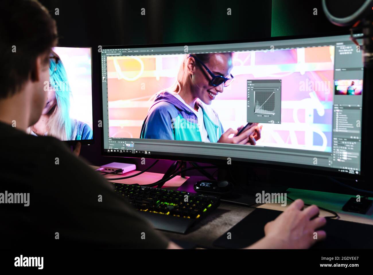 Back view of a young white man video editor sitting in front of a big ...