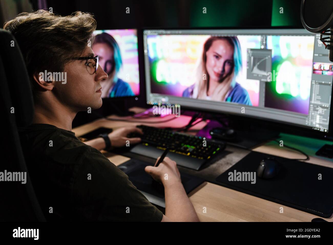Back view of a young white man video editor sitting in front of a big ...