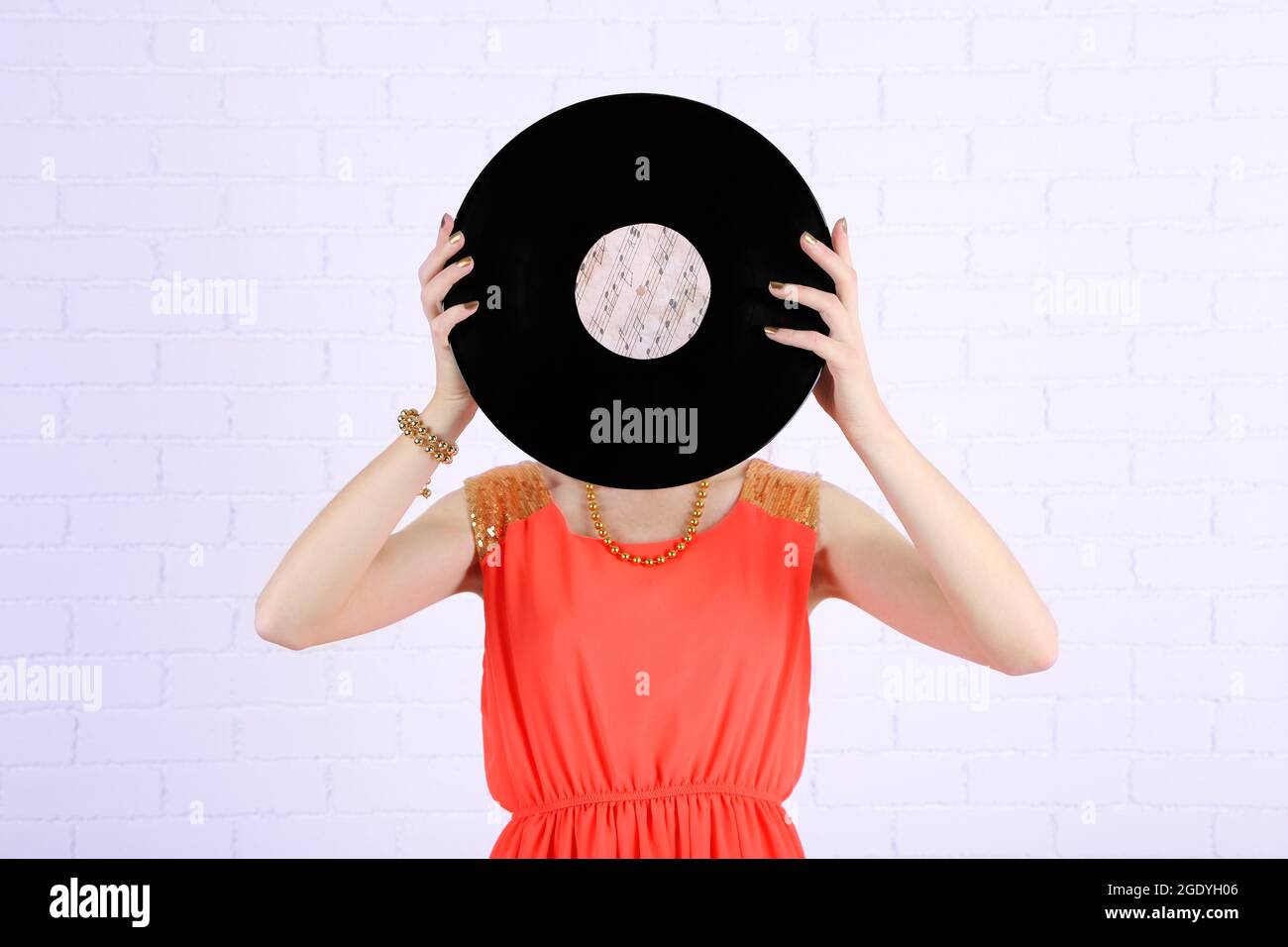 Young woman holding retro record in front of face, on shiny background ...
