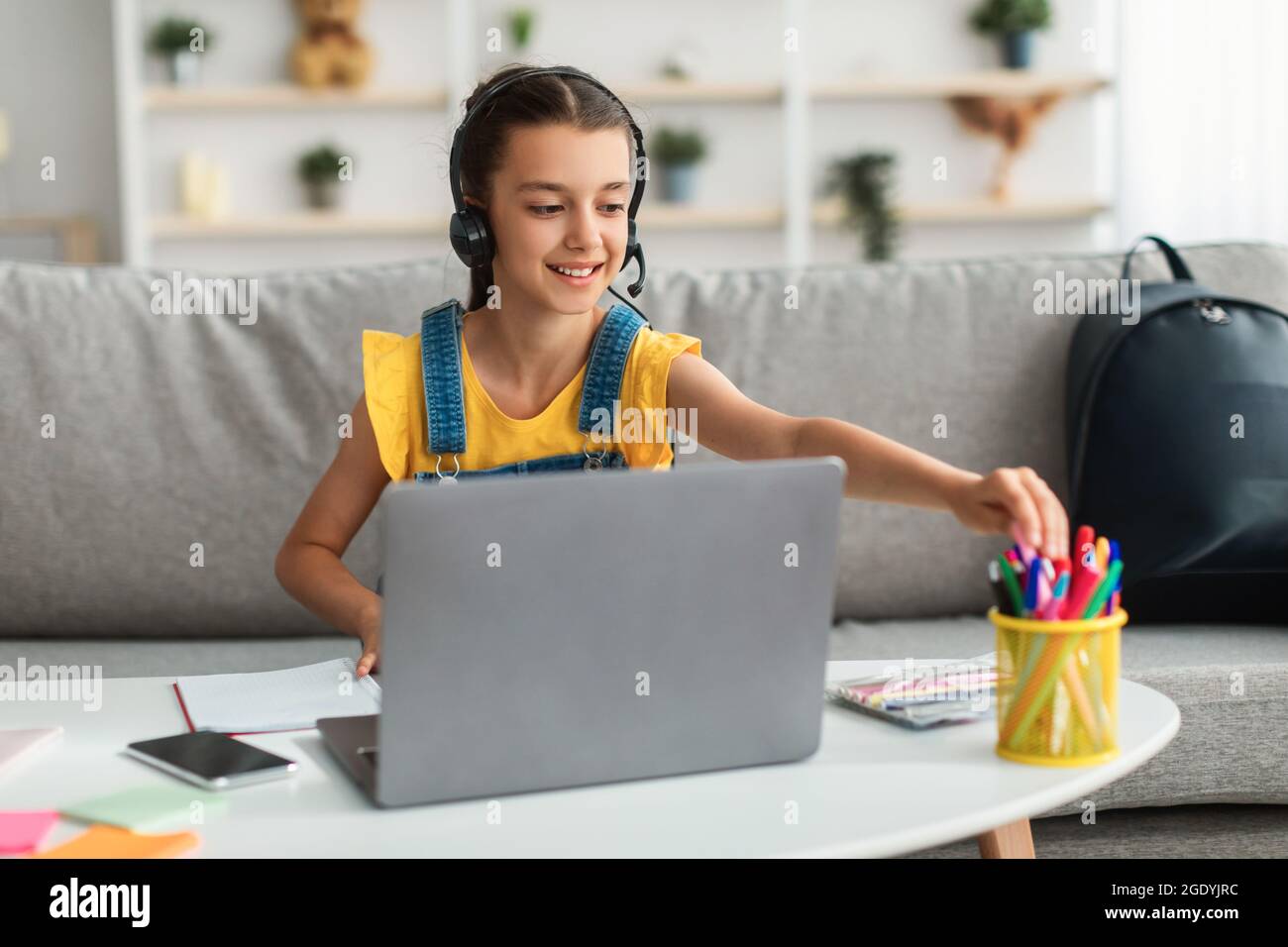Online Education. Girl using laptop, taking pen from pencil holder ...