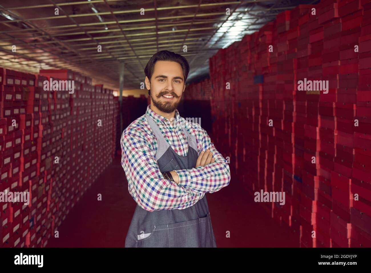 Footwear factory warehouse worker smiling at camera standing among shoe ...