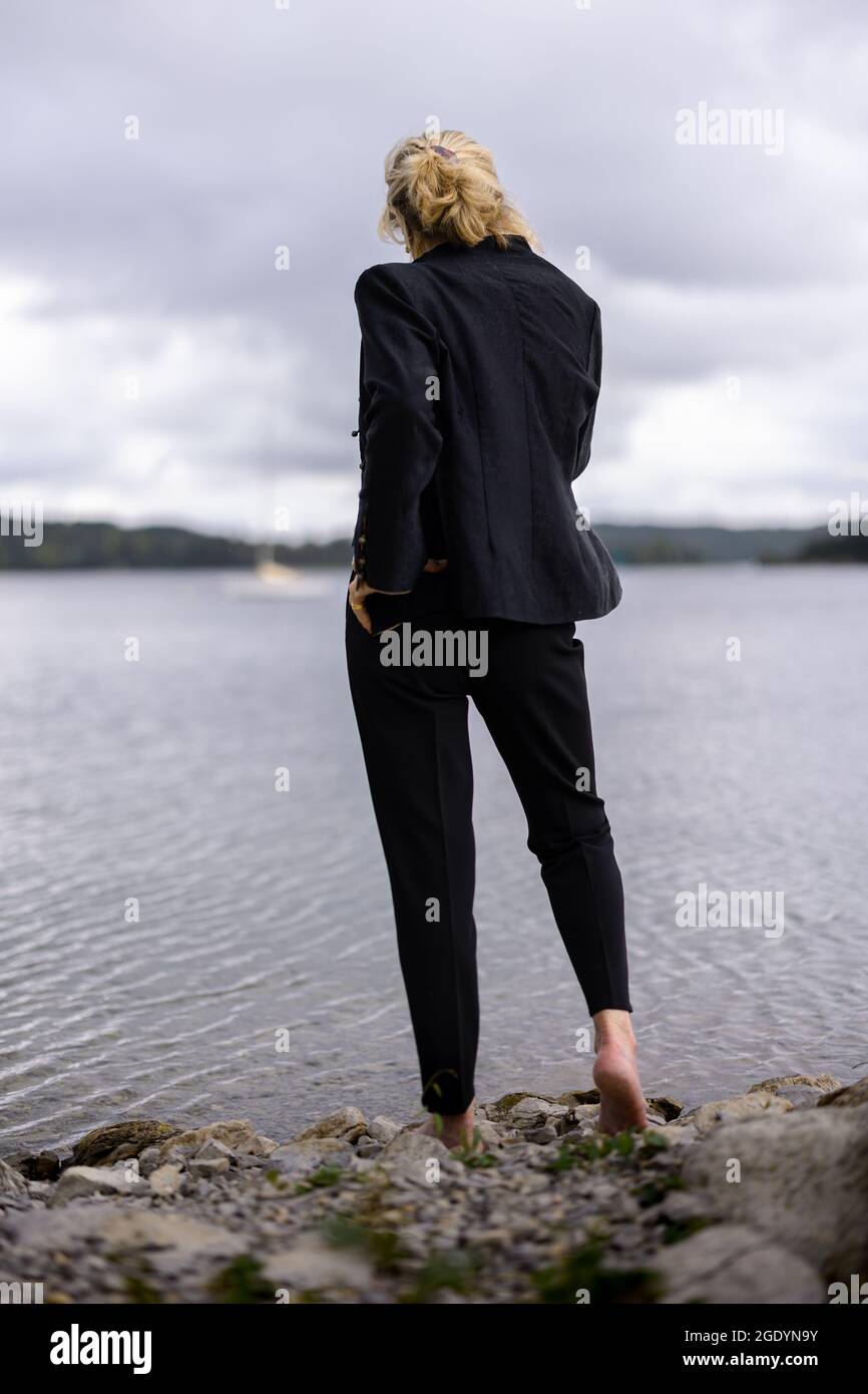 A back view of a cool barefoot woman in a black suit standing near a ...