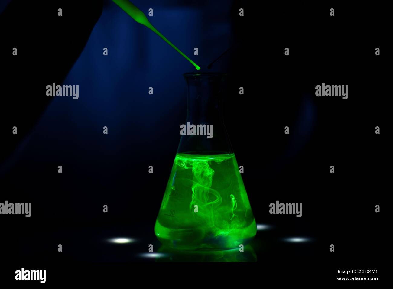 A researcher working with a green fluorescent compound in a glass ...