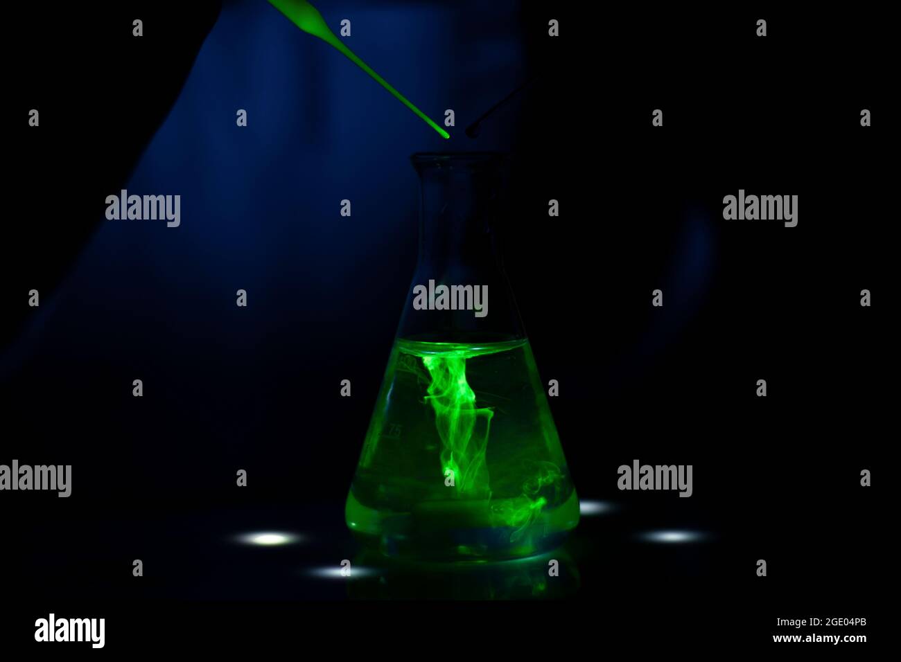 A scientist working with a green fluorescent compound in dark chemistry ...