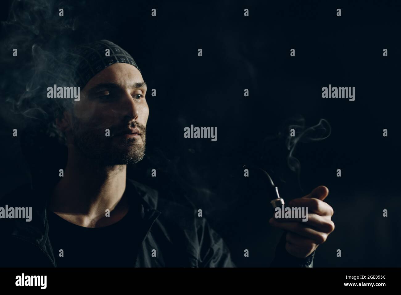 Man smokes smoking pipe against dark background. Back side lit profile ...