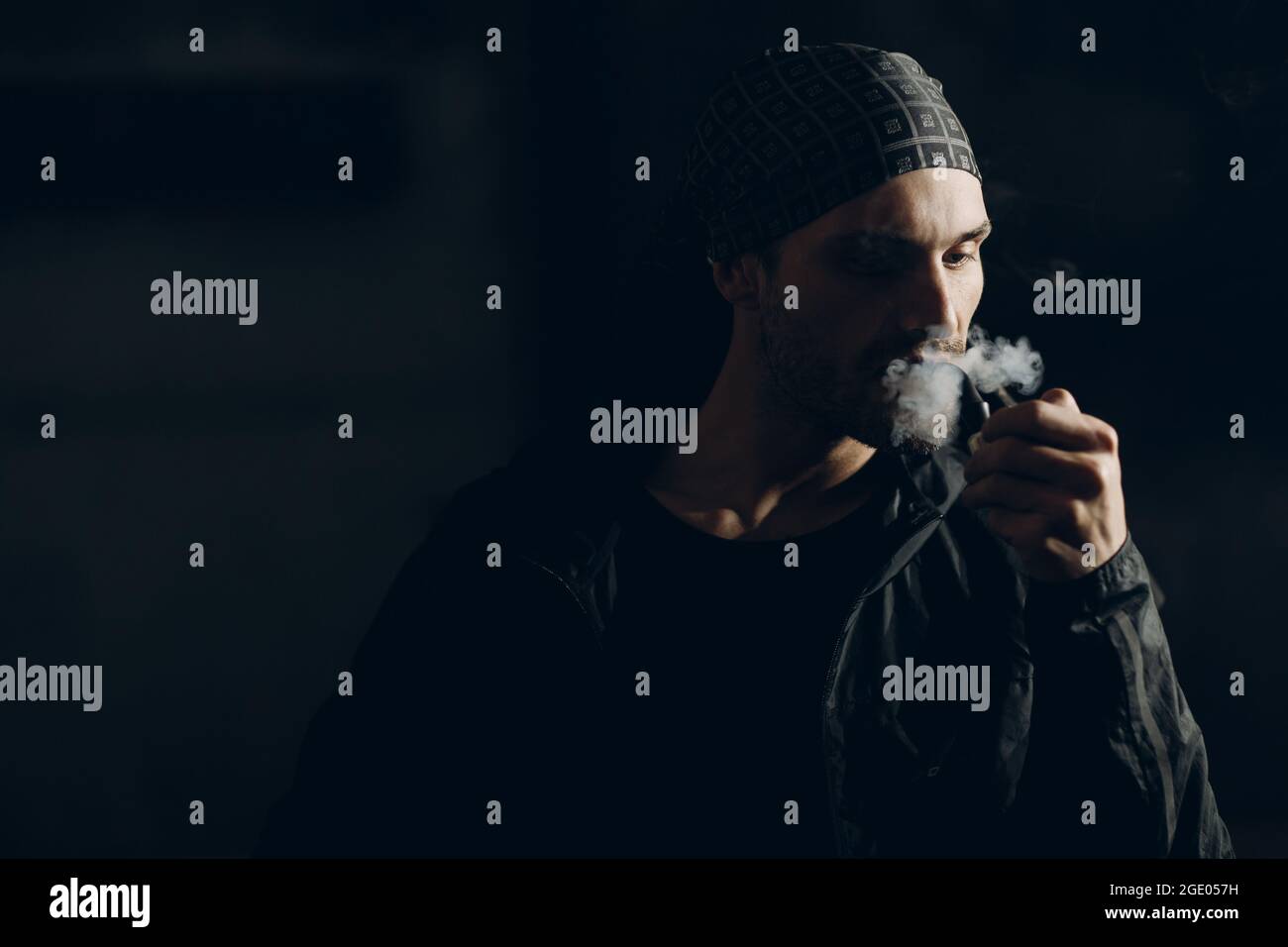 Man smokes smoking pipe against dark background. Back side lit profile ...