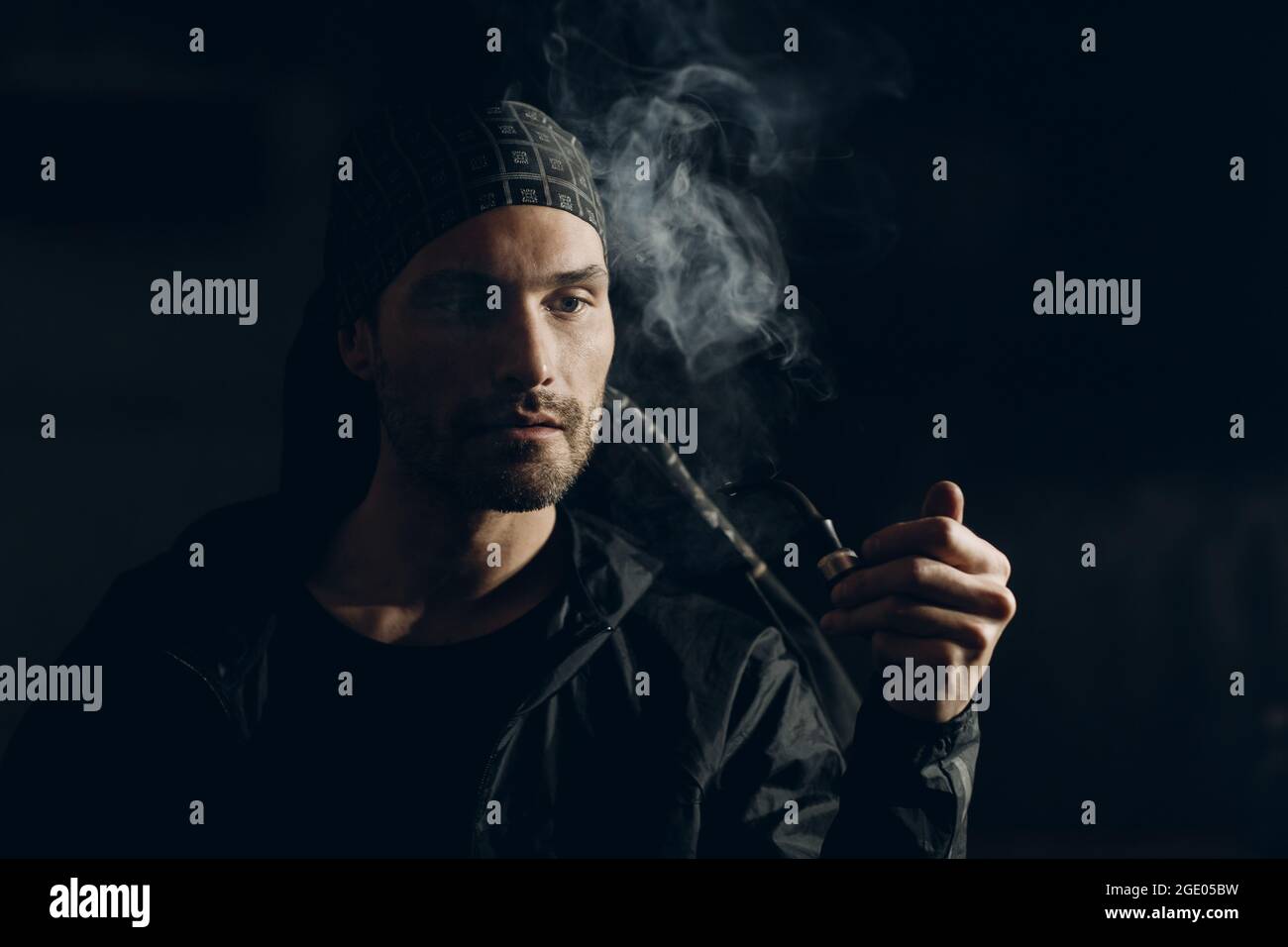 Man smokes smoking pipe against dark background. Back side lit profile ...