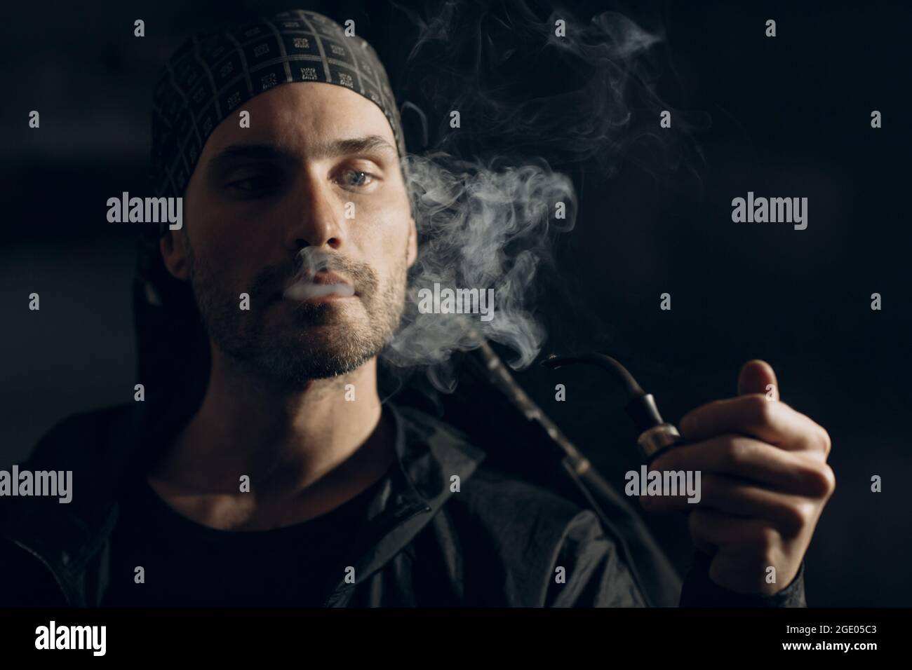 Man smokes smoking pipe against dark background. Back side lit profile ...