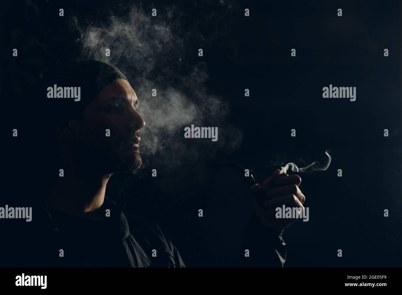 Man smokes smoking pipe against dark background. Back side lit profile ...