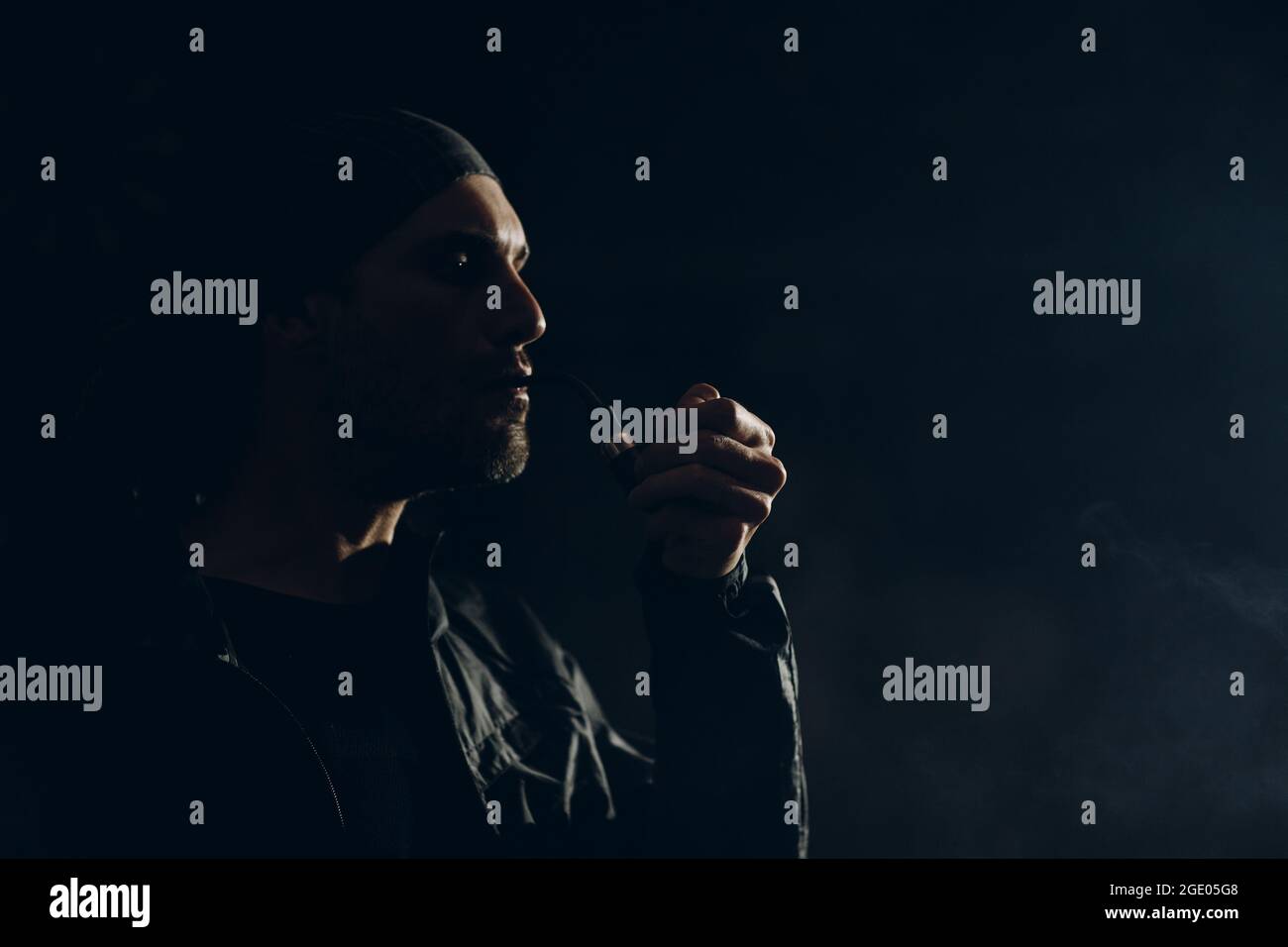 Man smokes smoking pipe against dark background. Back side lit profile ...