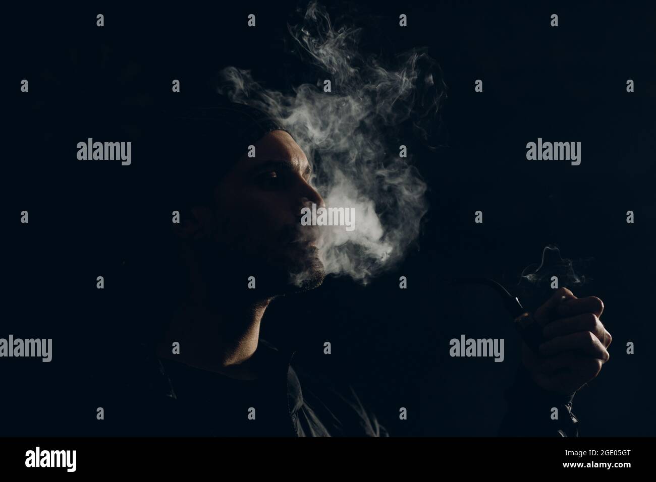 Man smokes smoking pipe against dark background. Back side lit profile ...