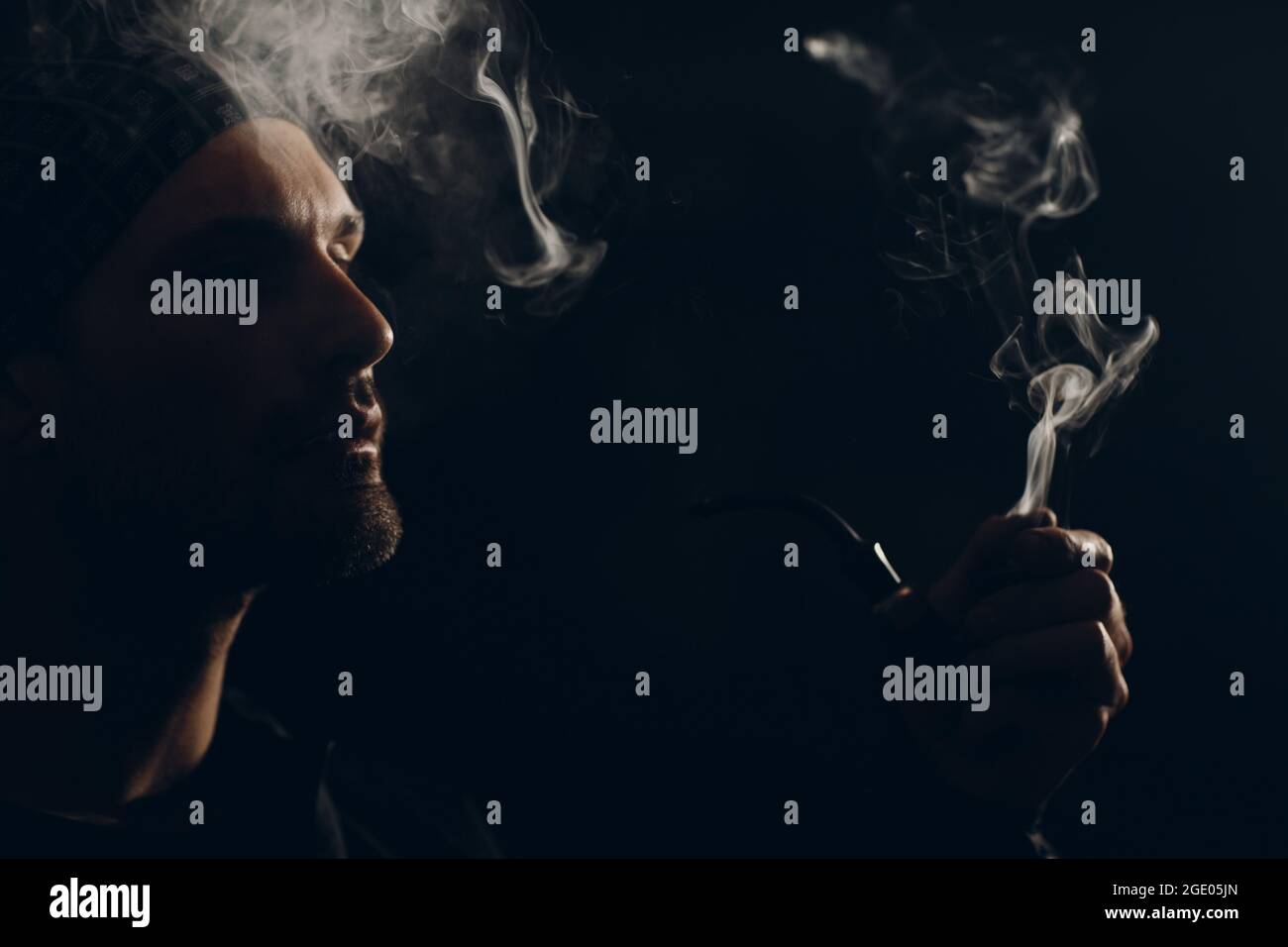 Man smokes smoking pipe against dark background. Back side lit profile ...