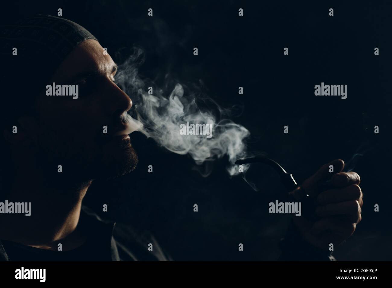Man smokes smoking pipe against dark background. Back side lit profile ...