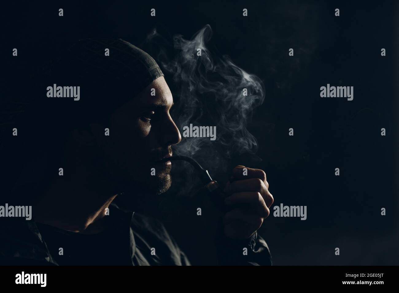 Man smokes smoking pipe against dark background. Back side lit profile ...