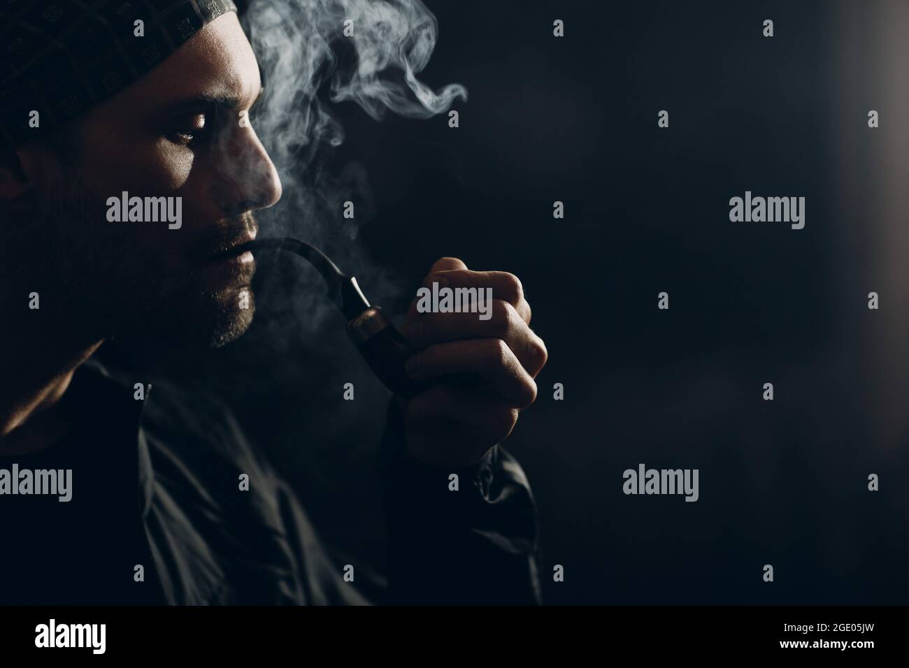 Man smokes smoking pipe against dark background. Back side lit profile ...