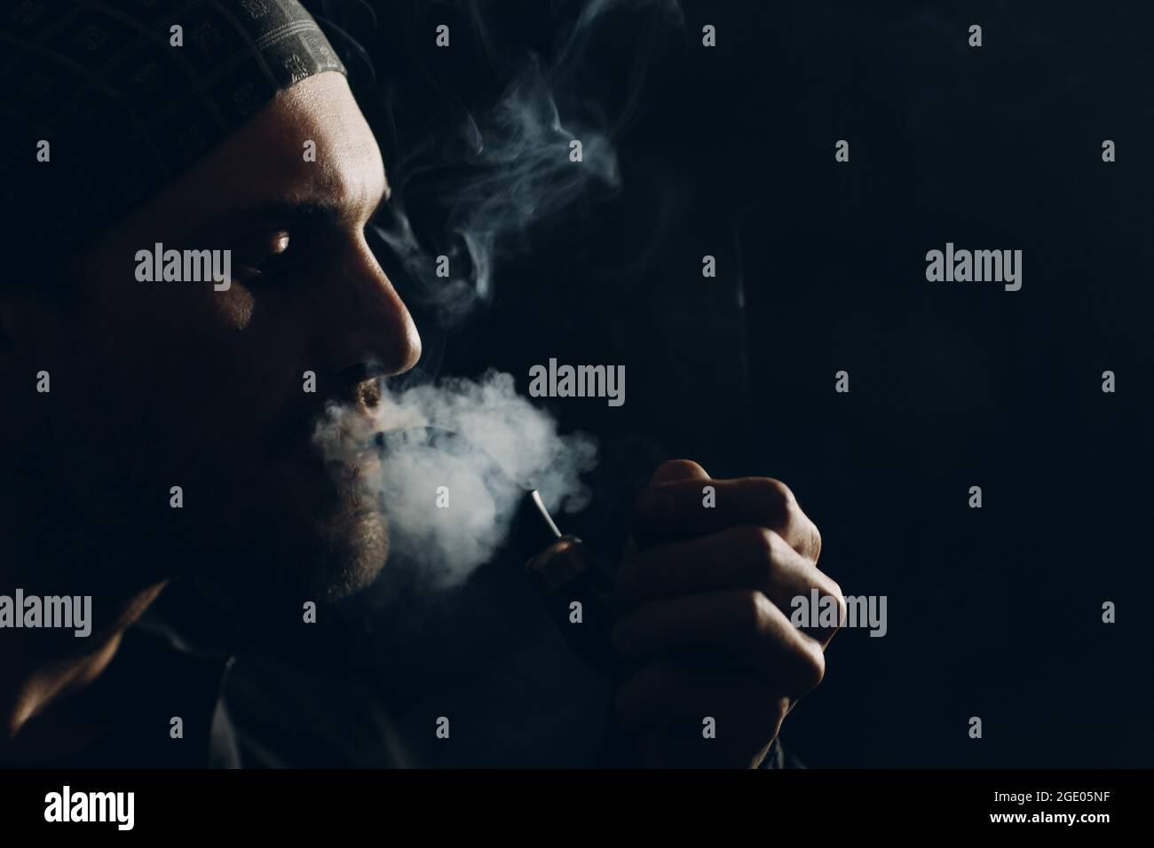 Man smokes smoking pipe against dark background. Back side lit profile ...