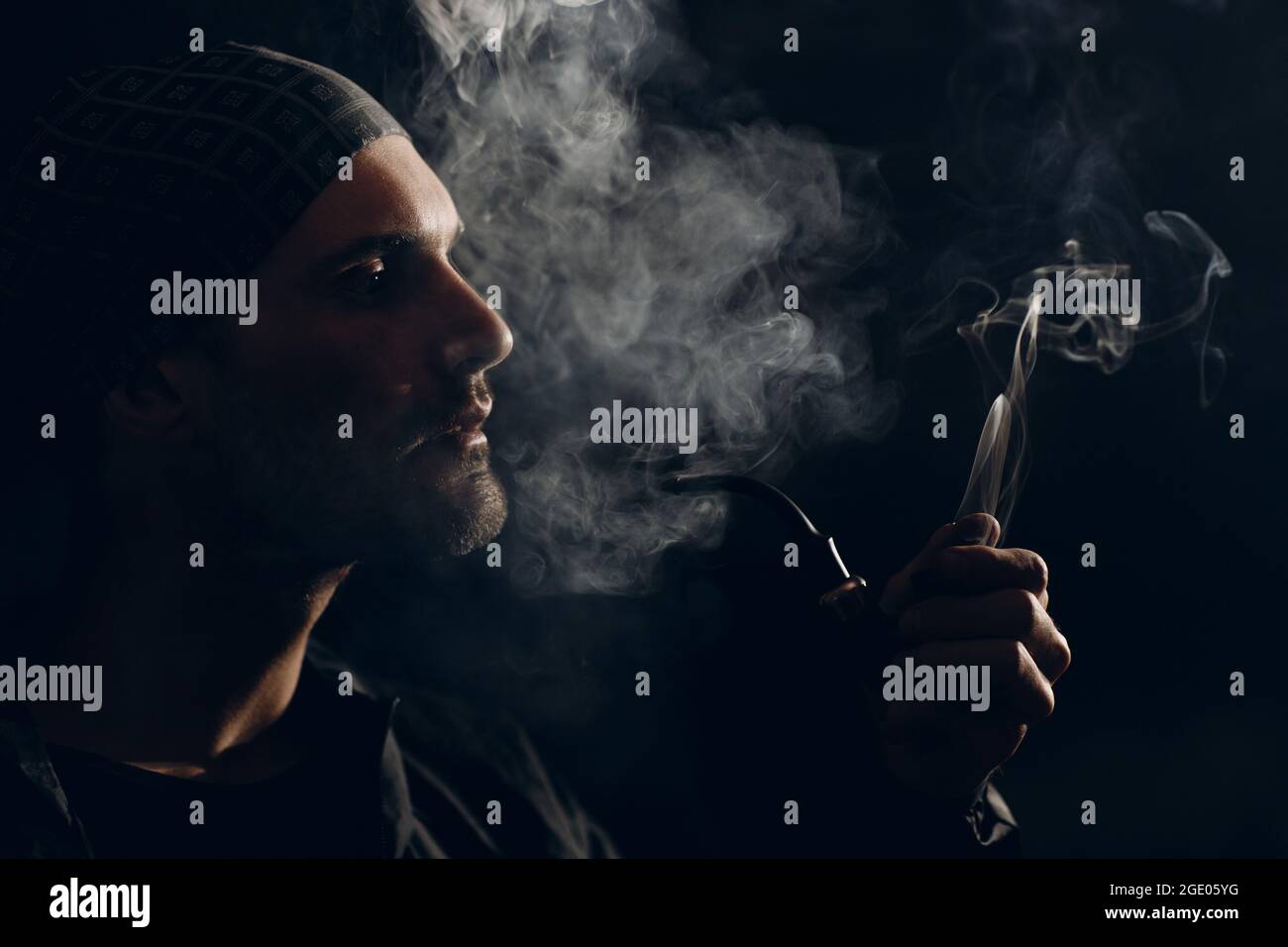 Man smokes smoking pipe against dark background. Back side lit profile ...