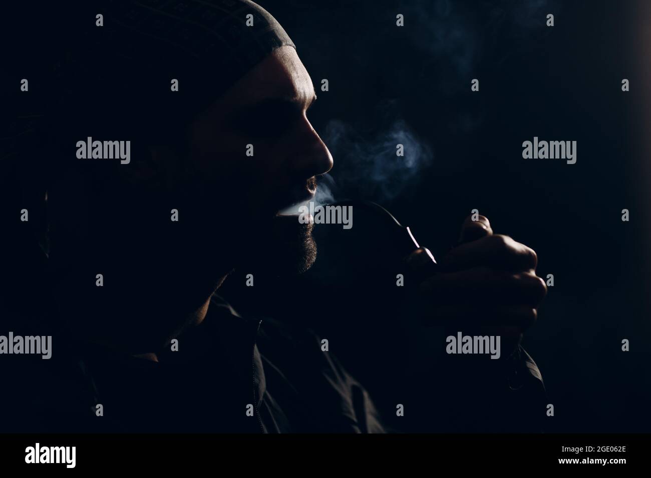 Man smokes smoking pipe against dark background. Back side lit profile ...