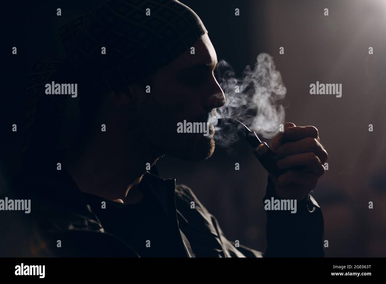Man smokes smoking pipe against dark background. Back side lit profile ...