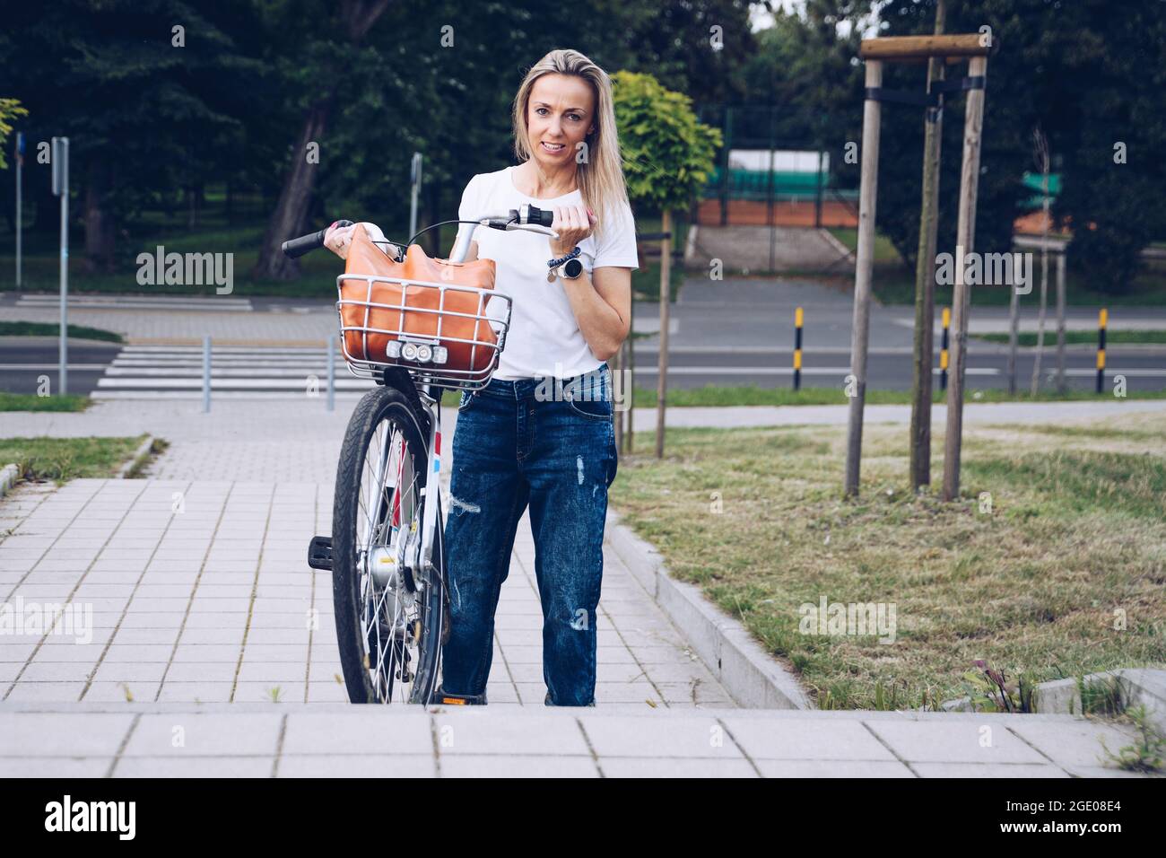 A worried woman in a white T-shirt climbs the stairs with a city bike Stock Photo - Alamy