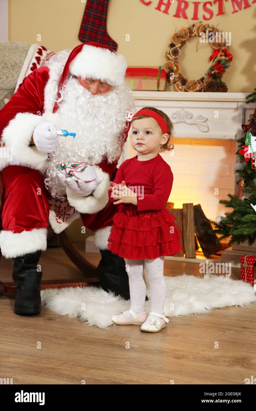 Santa Claus giving present to little cute girl near fireplace and ...