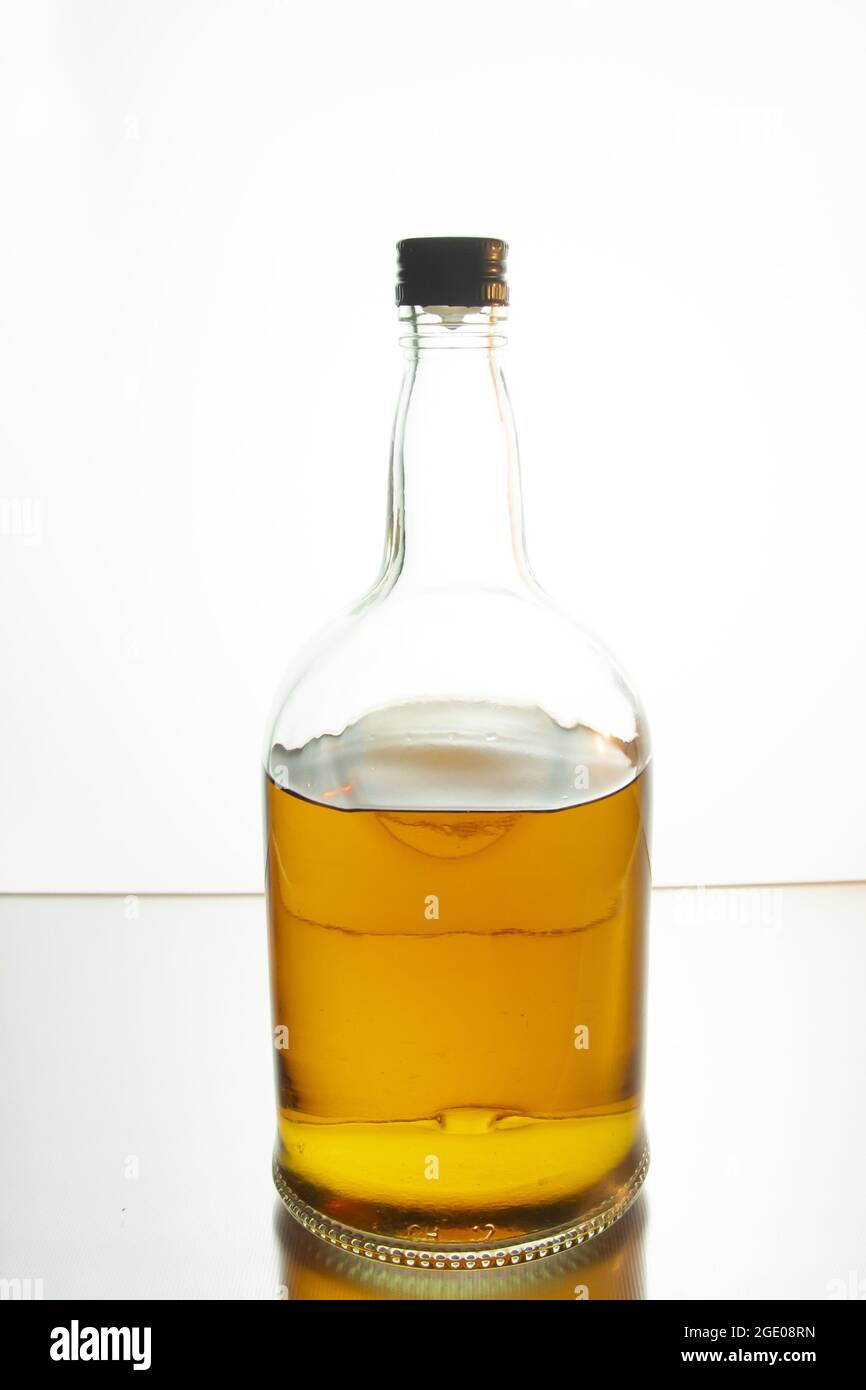 A bottle of amber-colored whisky on the table with bright background ...