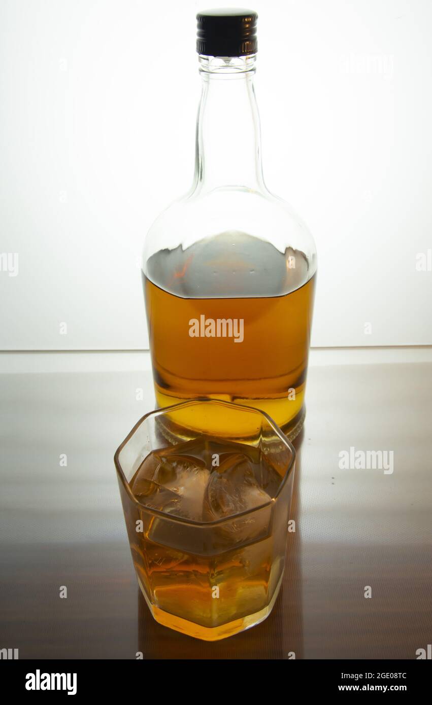 A bottle and a glass of amber-colored whisky on the table with bright ...